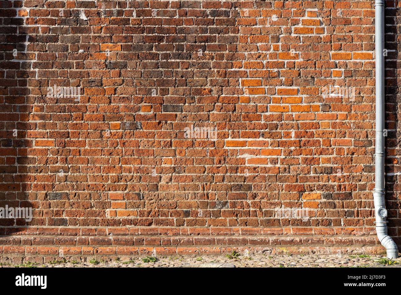 Old brick wall of a traditional building. The pipe of a roof gutter is ...