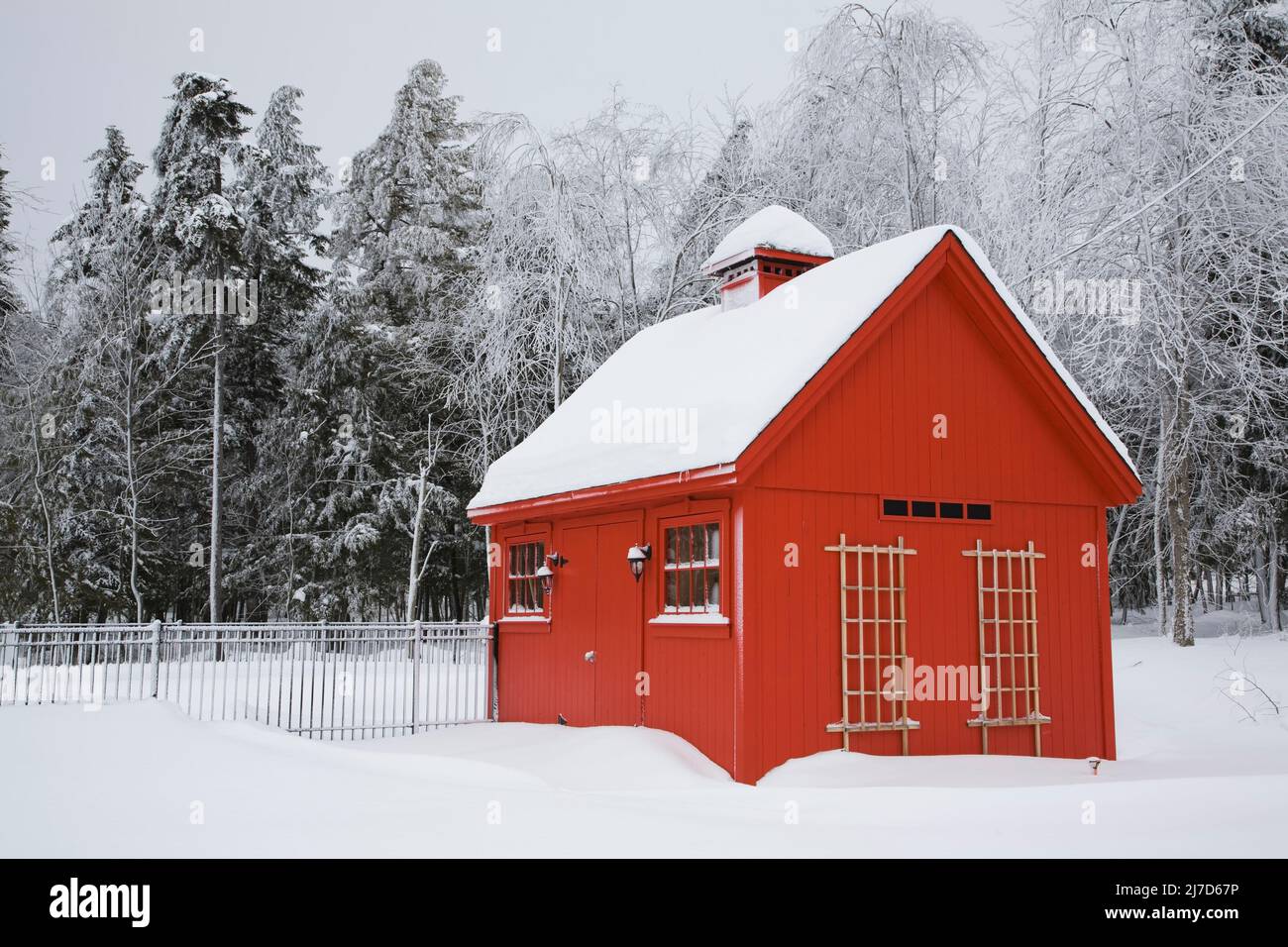 Red barn style storage shed with frost and snow covered trees in winter ...
