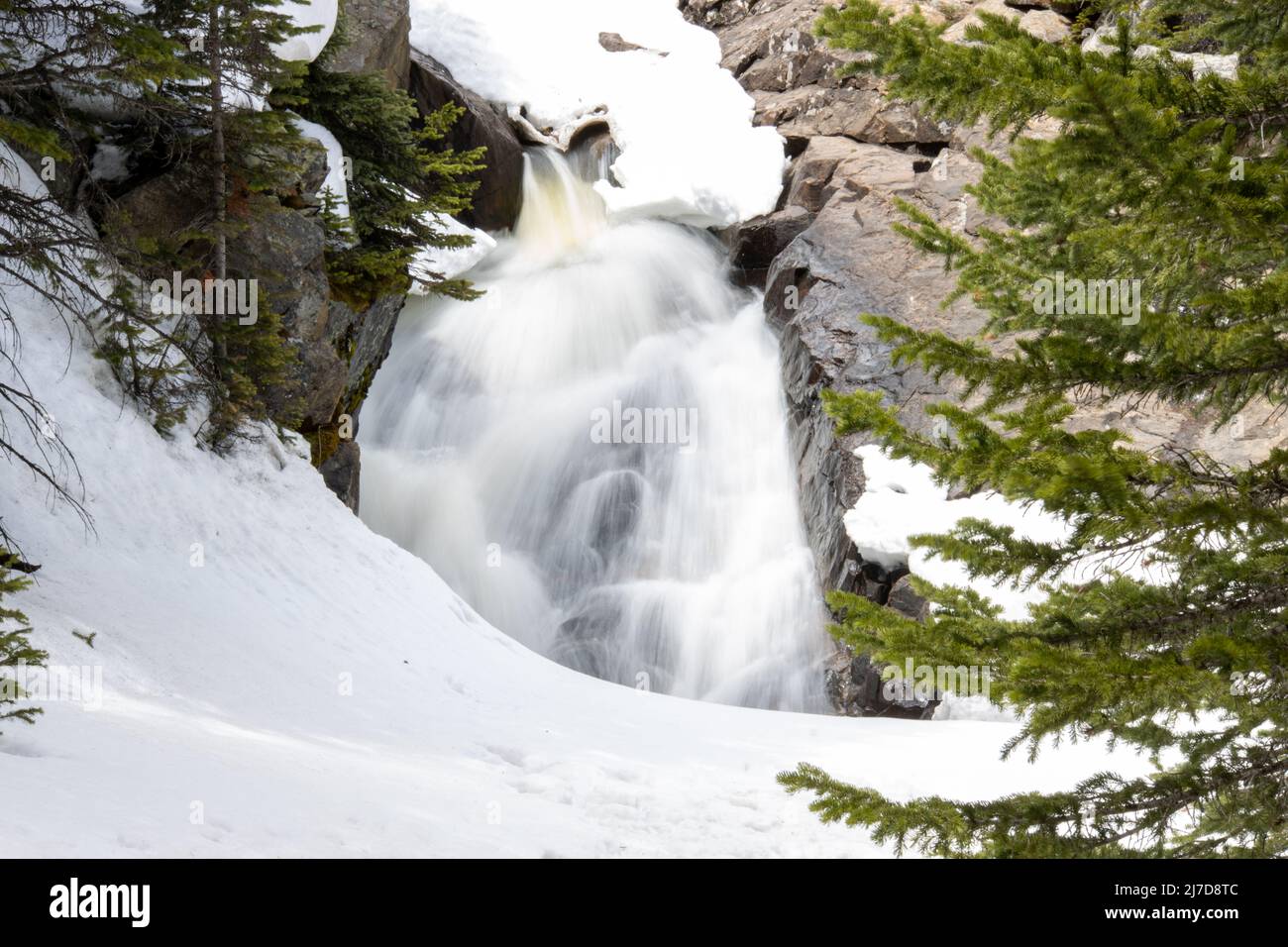 A waterfall cascades down a snowy mountain in the Rocky Mountains of ...