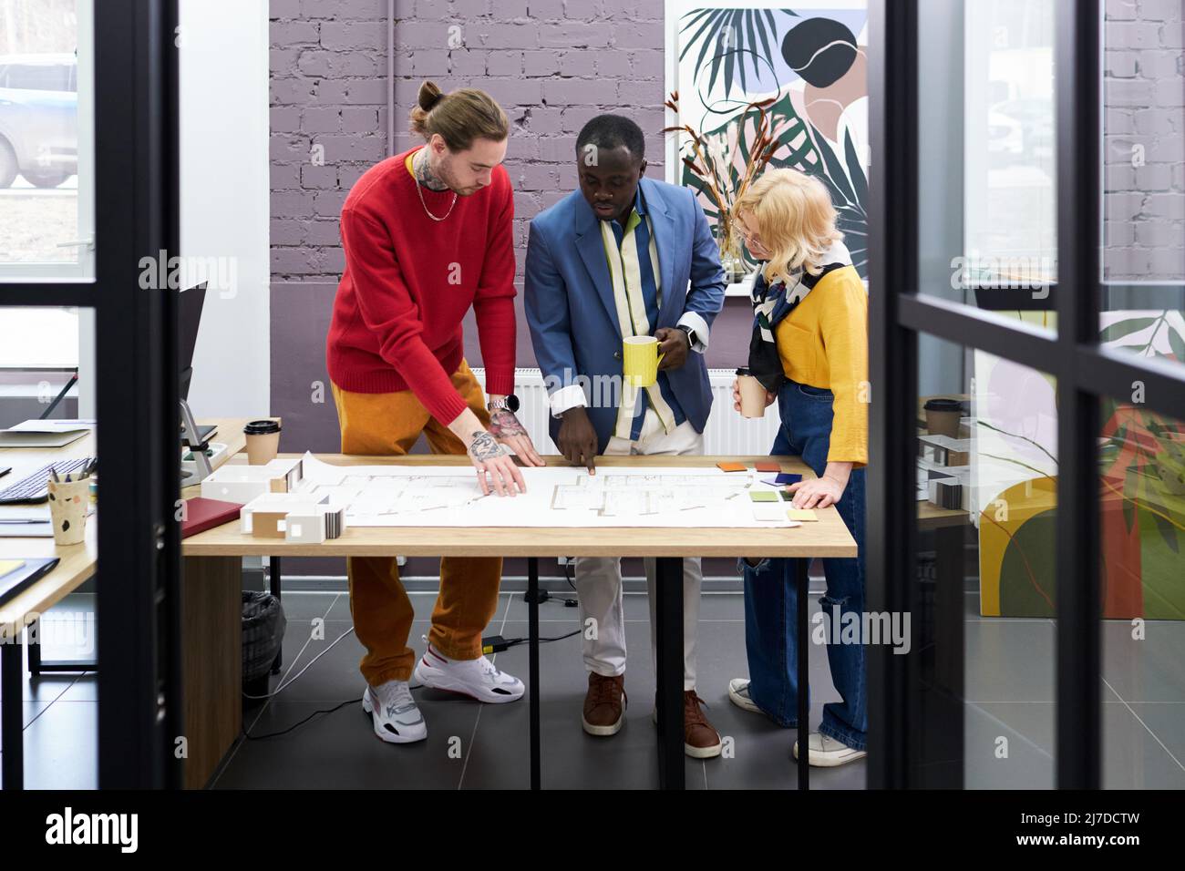 Group of architects standing at table and working over blueprint in ...