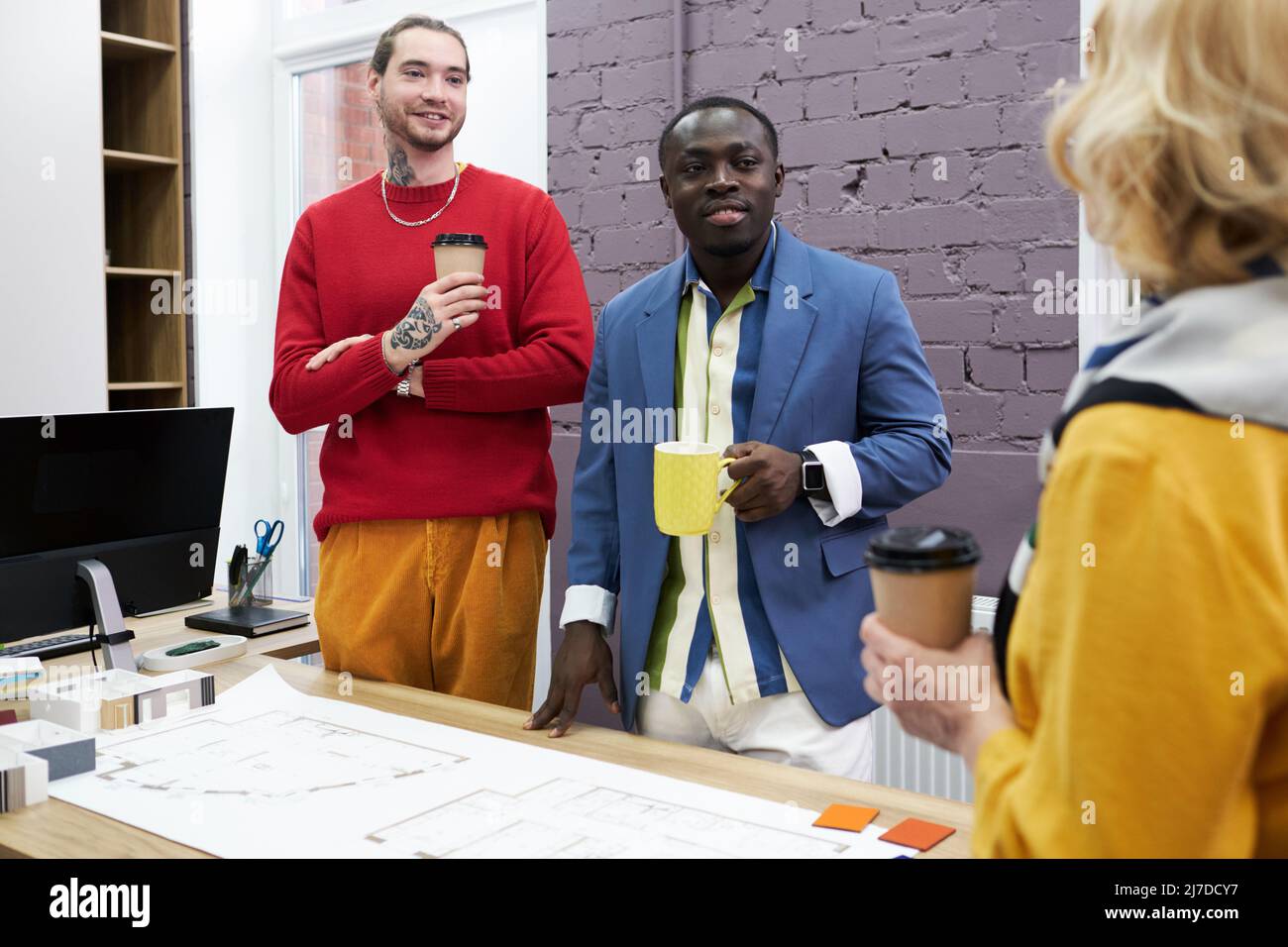 Two businessmen standing with coffee and talking to their colleague ...