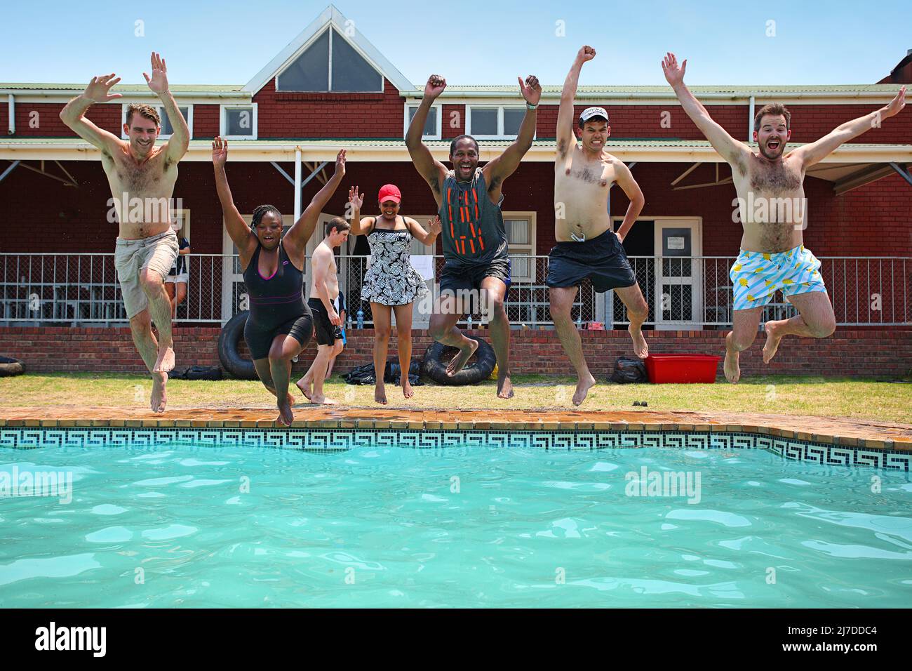 Six students mid-air jumping into the pool at the GSB team-building ...