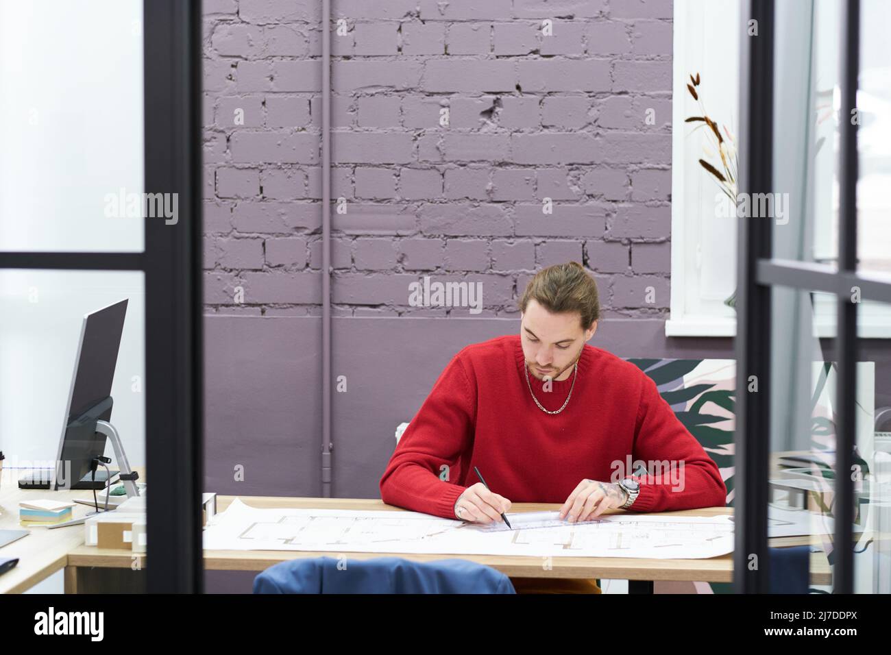 Young designer sitting at his workplace at office and busy with drawing ...
