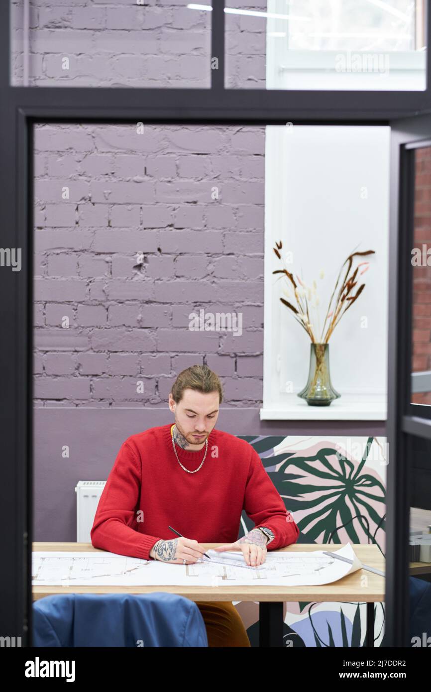 Young architect using ruler to draw blueprint of new construction ...