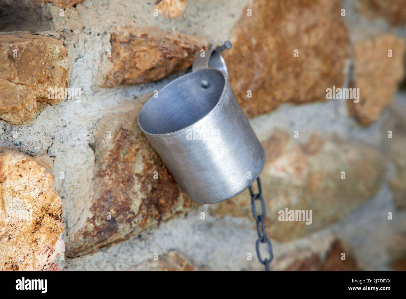 Aluminum mug hanging on a chain on a stone wall Stock Photo - Alamy