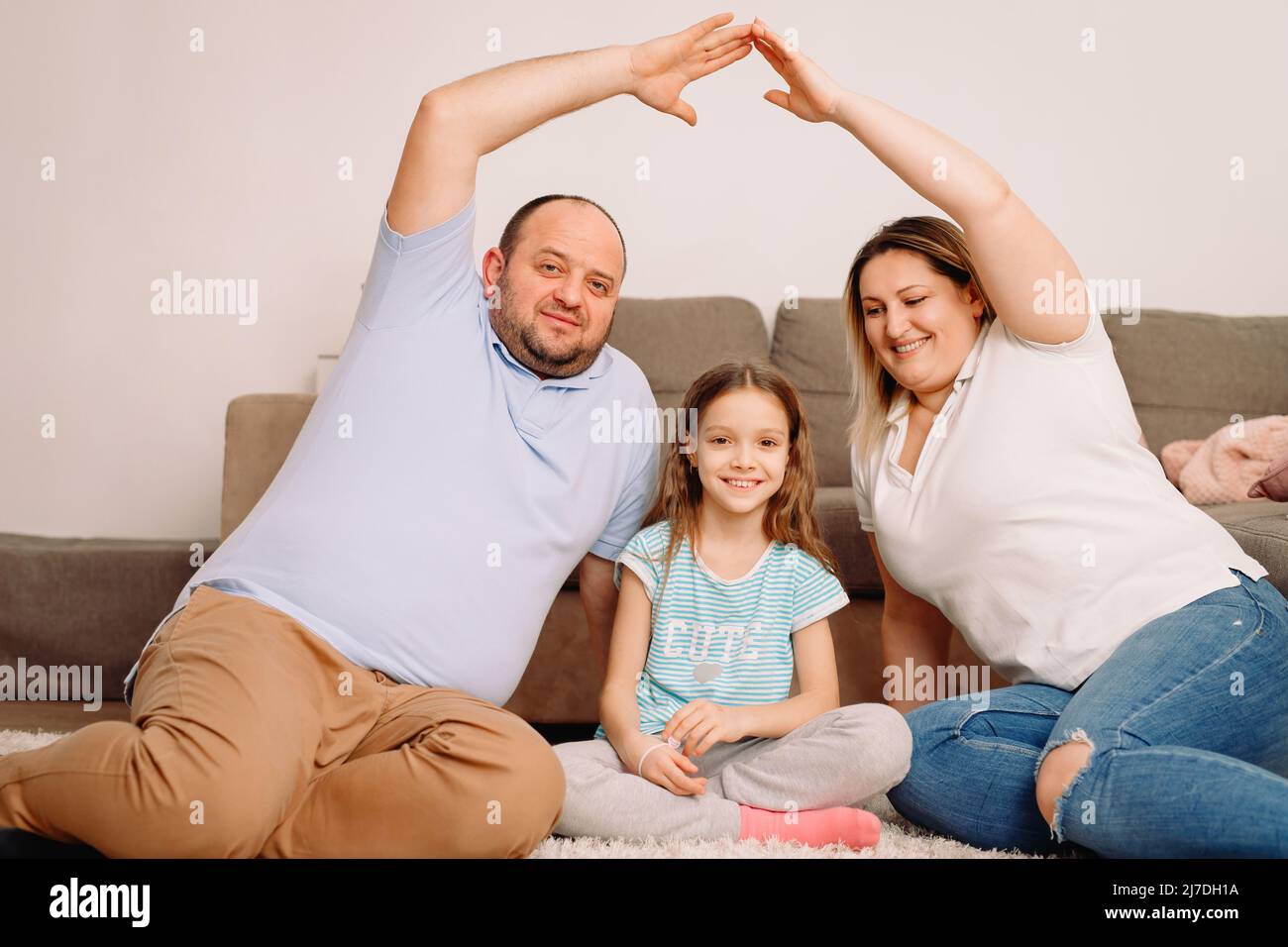 Happy family of three persons sitting together on the carpet with ...