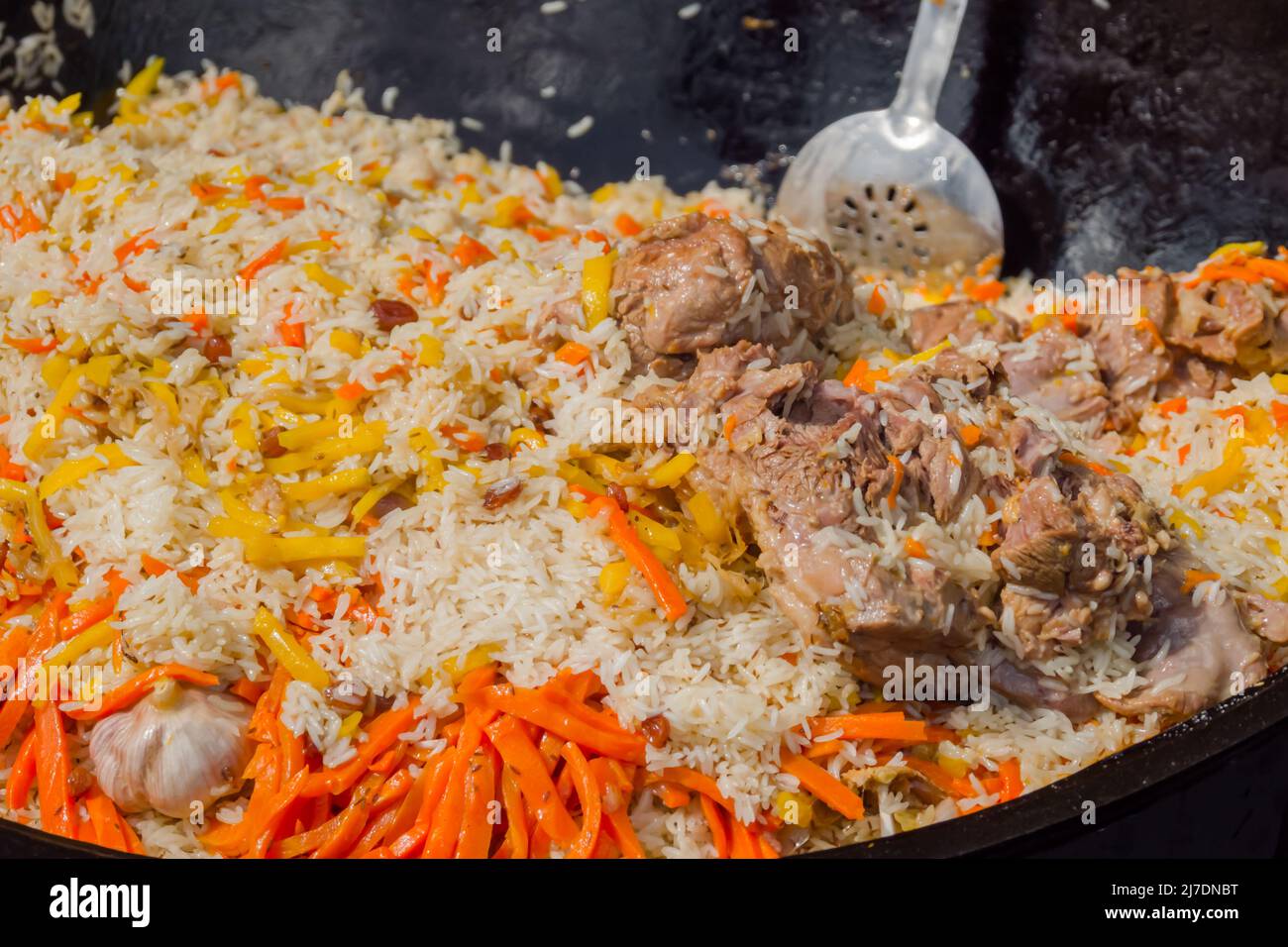 Process of cooking pilaf in huge cauldron at summer outdoor food market ...