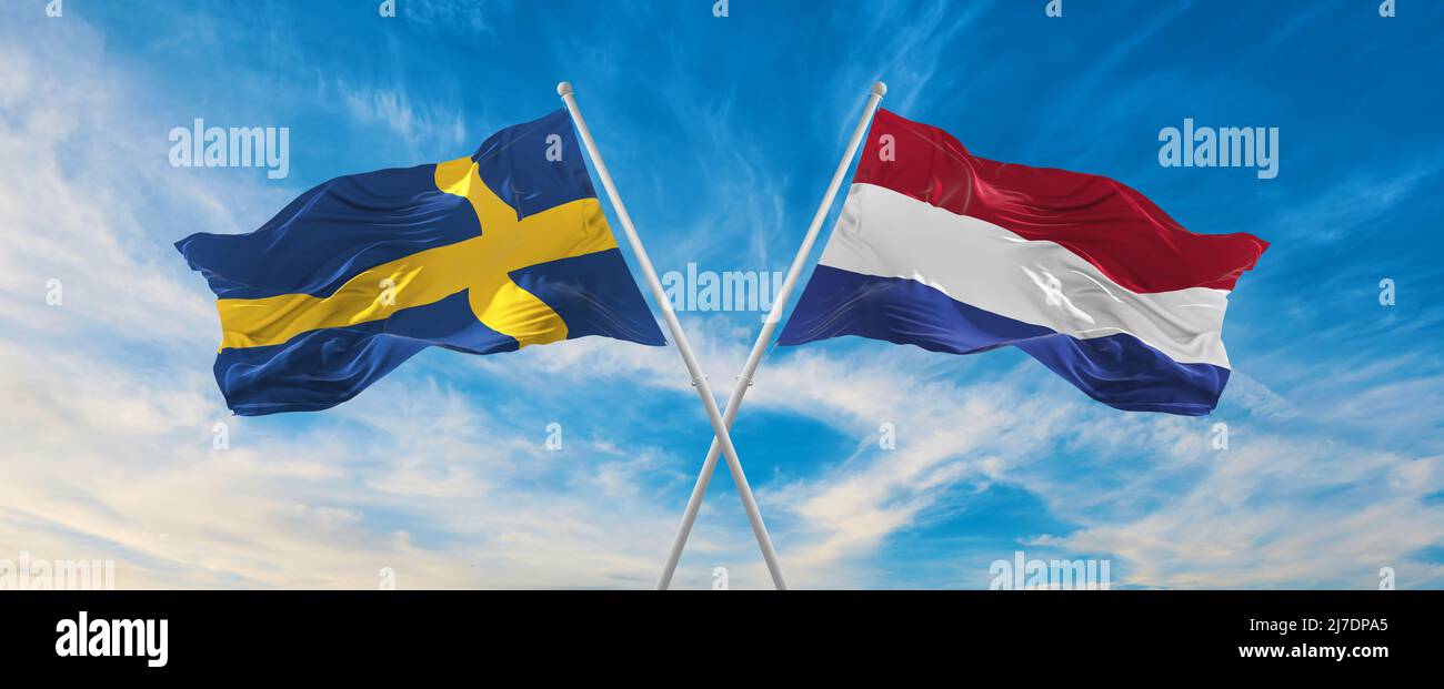 two crossed flags SWEDEN and Netherland waving in wind at cloudy sky ...