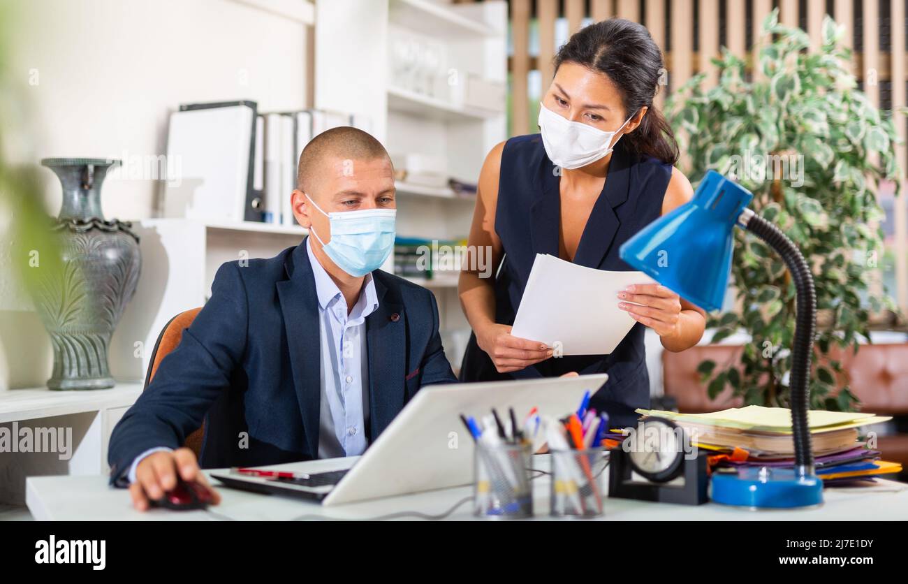 Two office employees in masks working with papers and laptop Stock ...