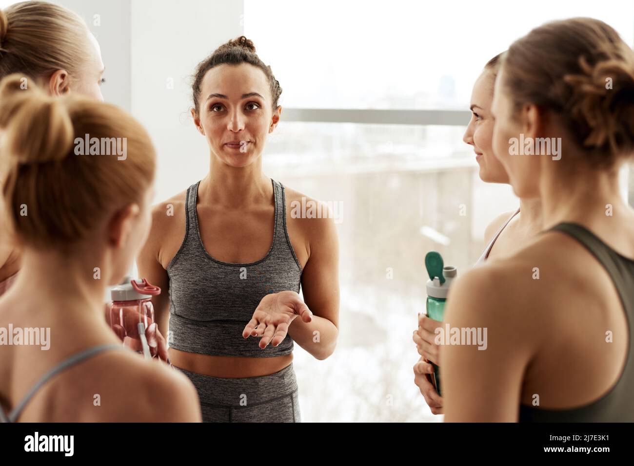 Group of fit girls standing in circle and drinking water while sharing ...