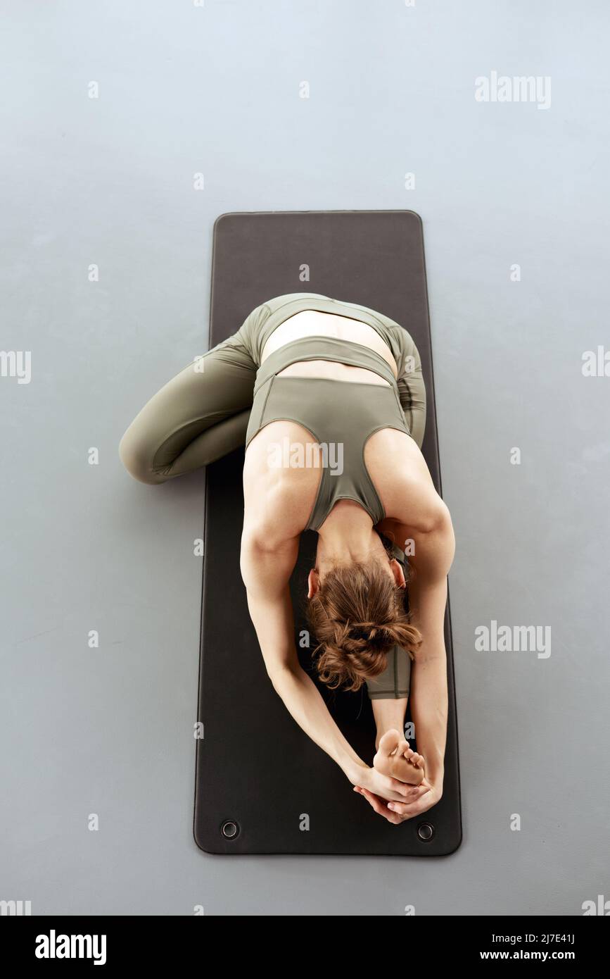 High angle view of woman sitting on mat and bending forward leg while ...