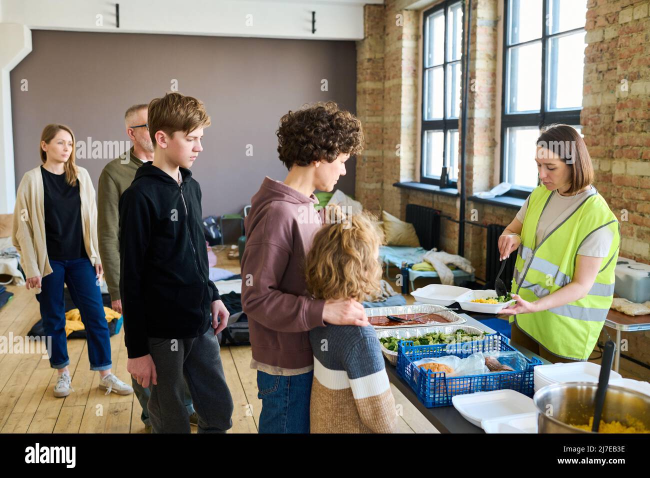 Group of refugees standing in queue in front of table with food cooked ...