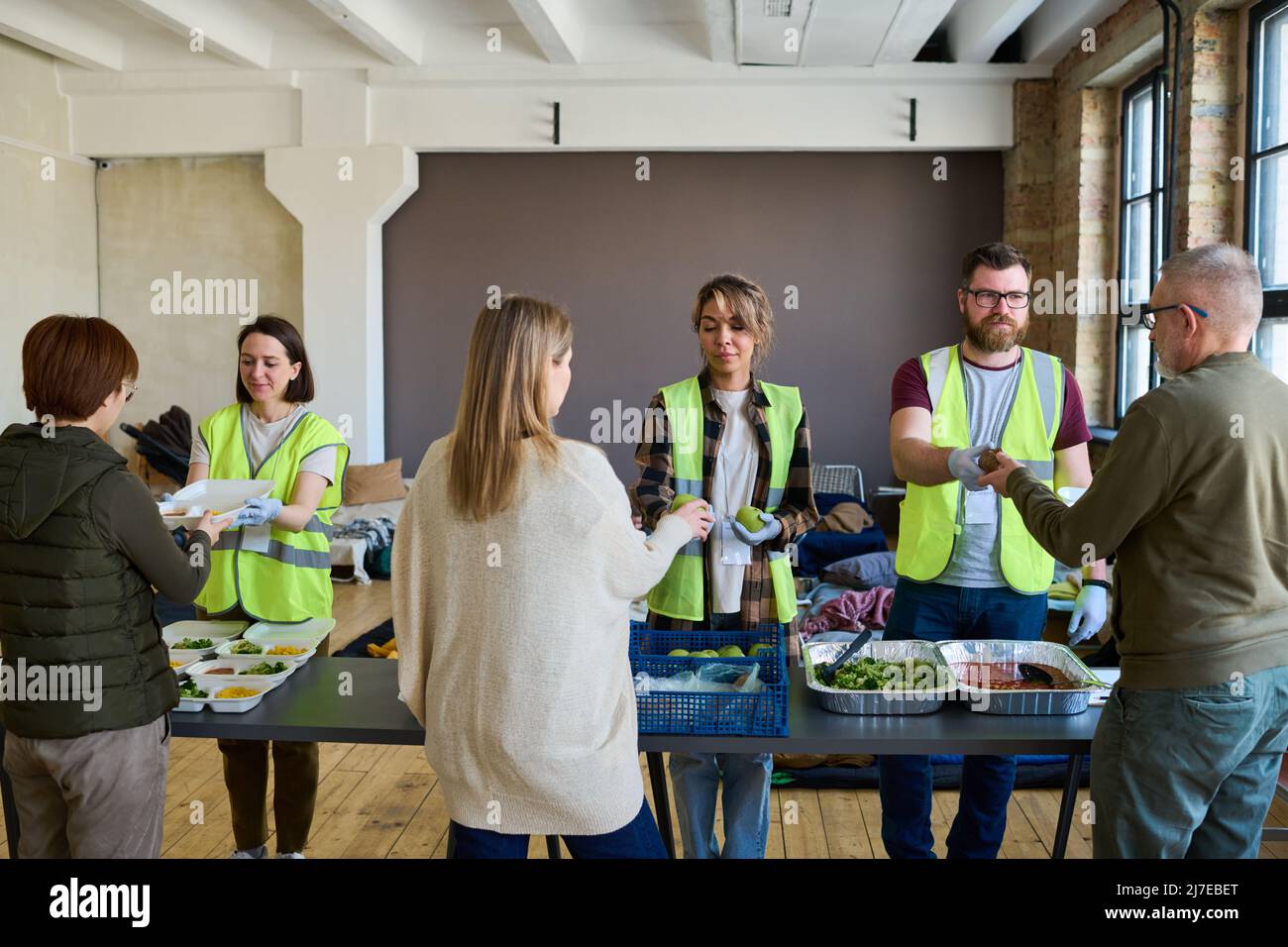 Group of volunteers standing by table with containers and boxes with ...