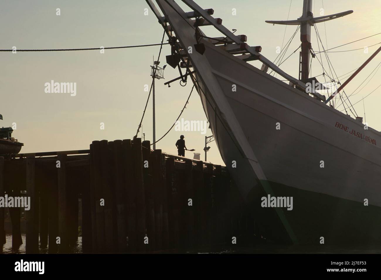 A traditional phinisi ship and silhouette of a worker standing on a ...