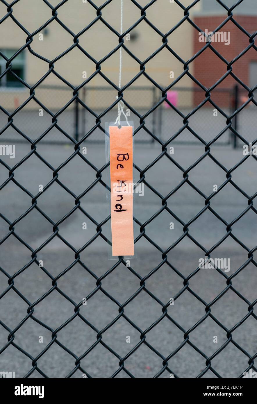 A laminated note card (Be Kind)is hanging from a chain link fence in a ...