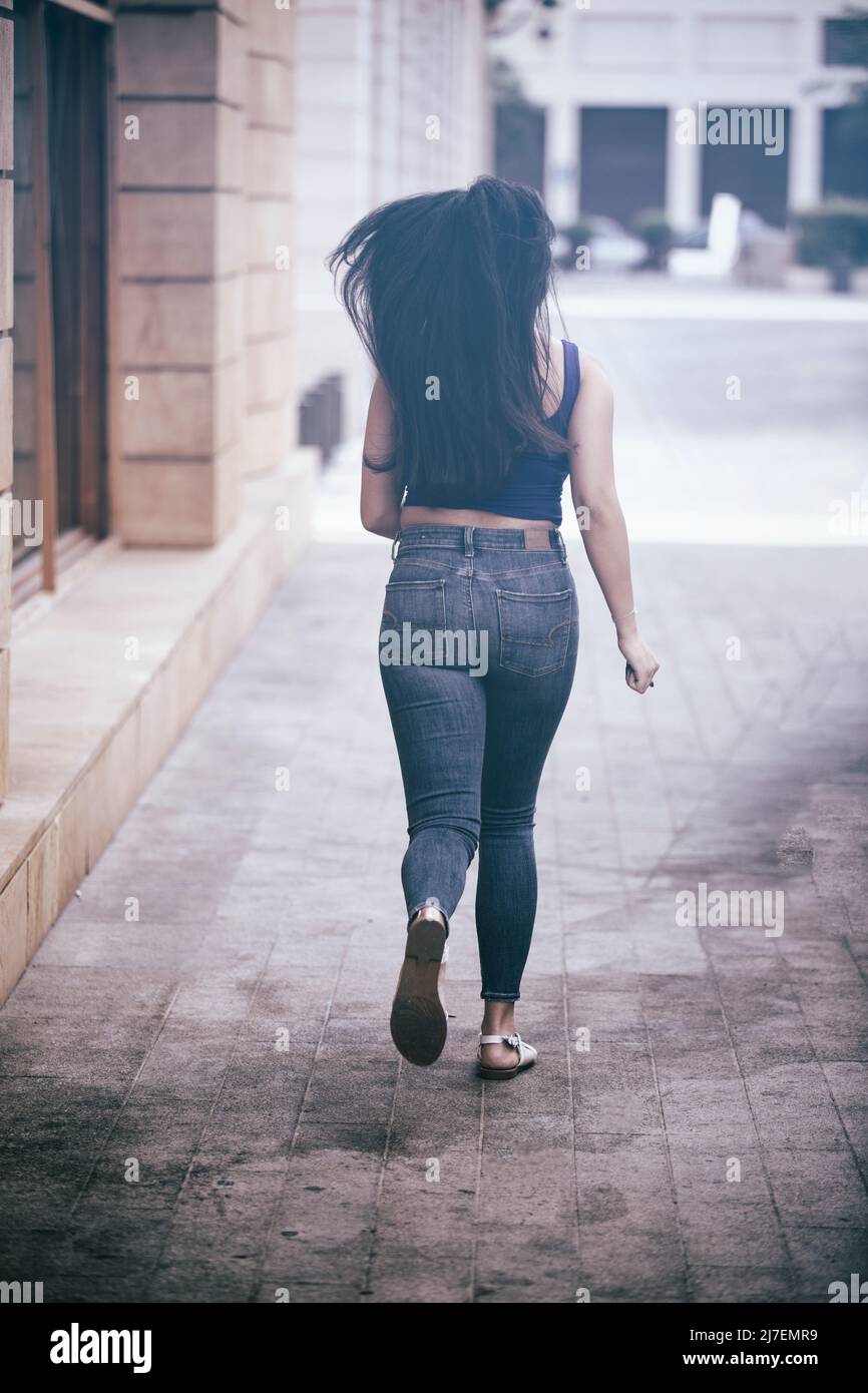 Rear view of woman in danger running away in the street Stock Photo - Alamy