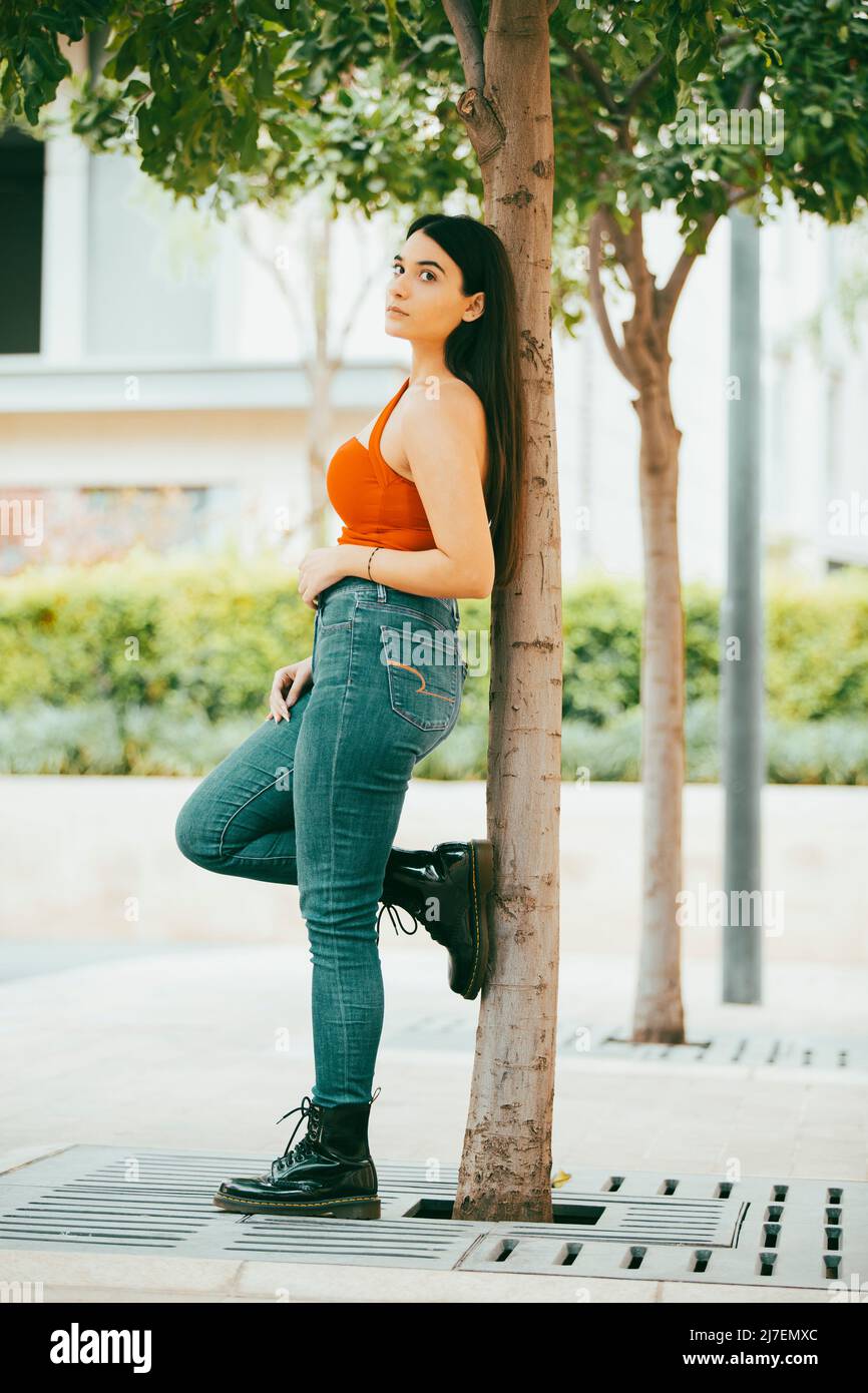 Beautiful woman leaning against a tree looking away Stock Photo - Alamy