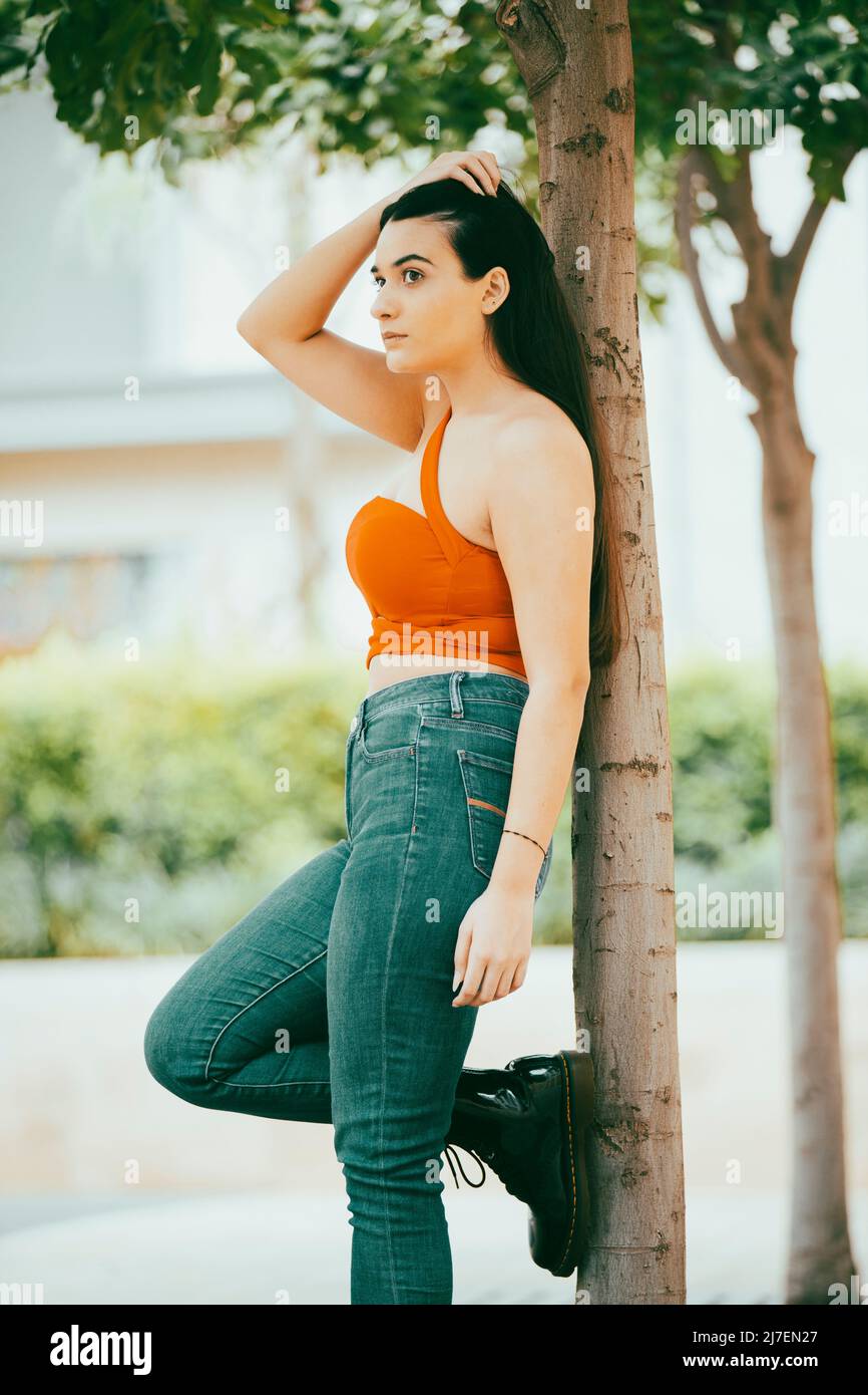 Beautiful woman leaning against a tree looking away Stock Photo - Alamy