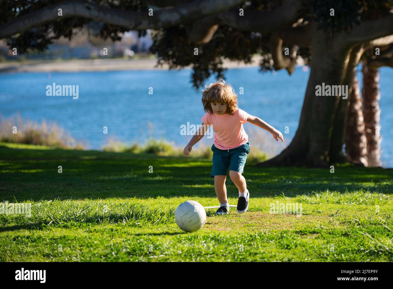 Boy child kicking football on the sports field during soccer match ...