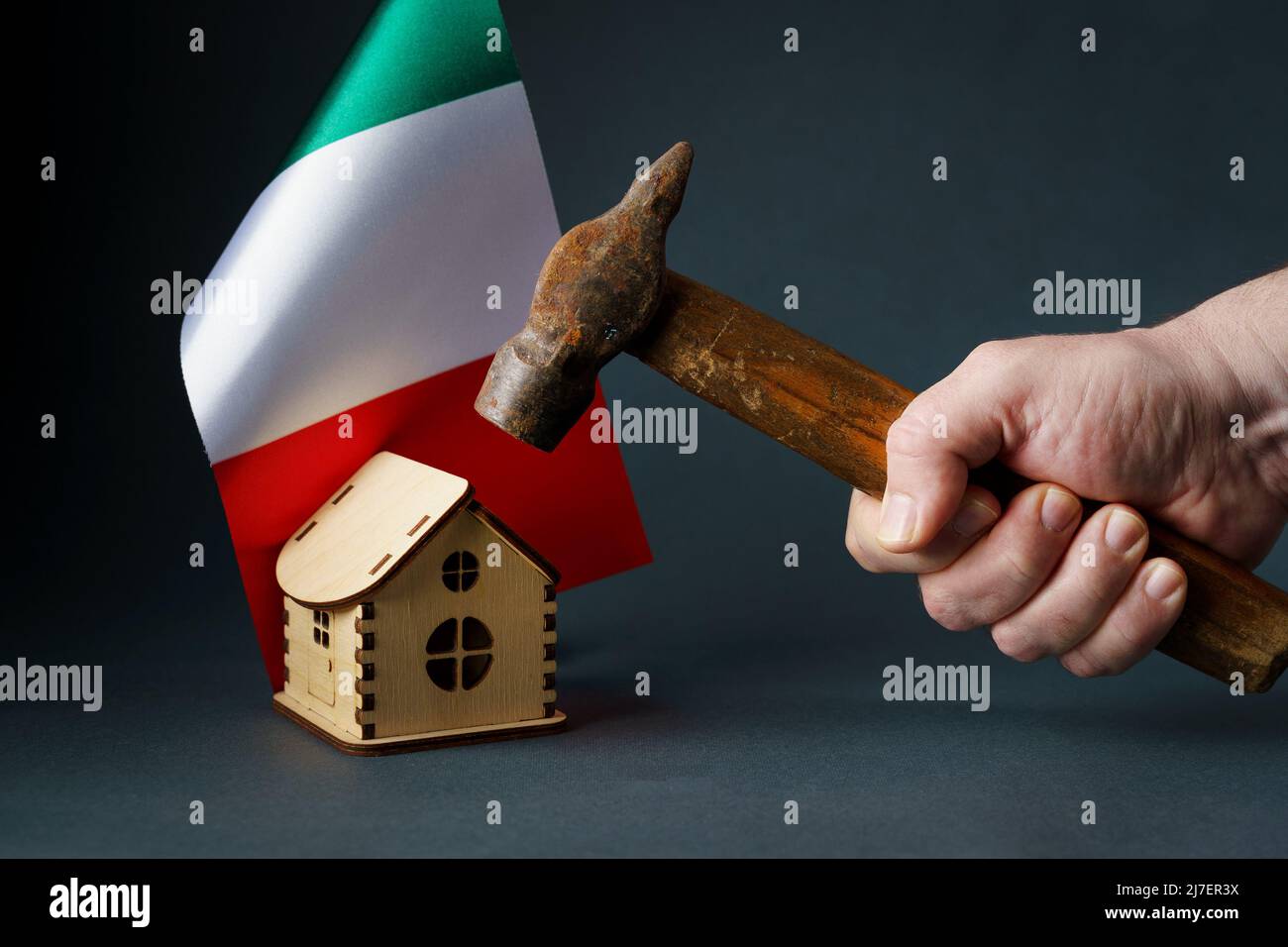A hammer is raised above the house with the flag of Italy. An old rusty ...