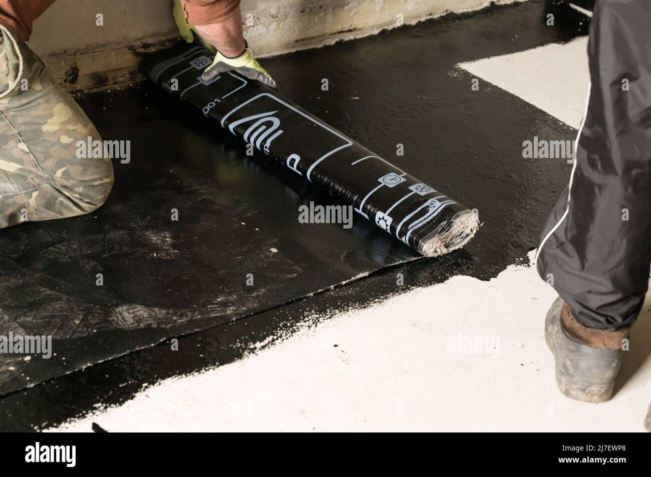 The worker untwists the roll of waterproofing and fastens it to the ...