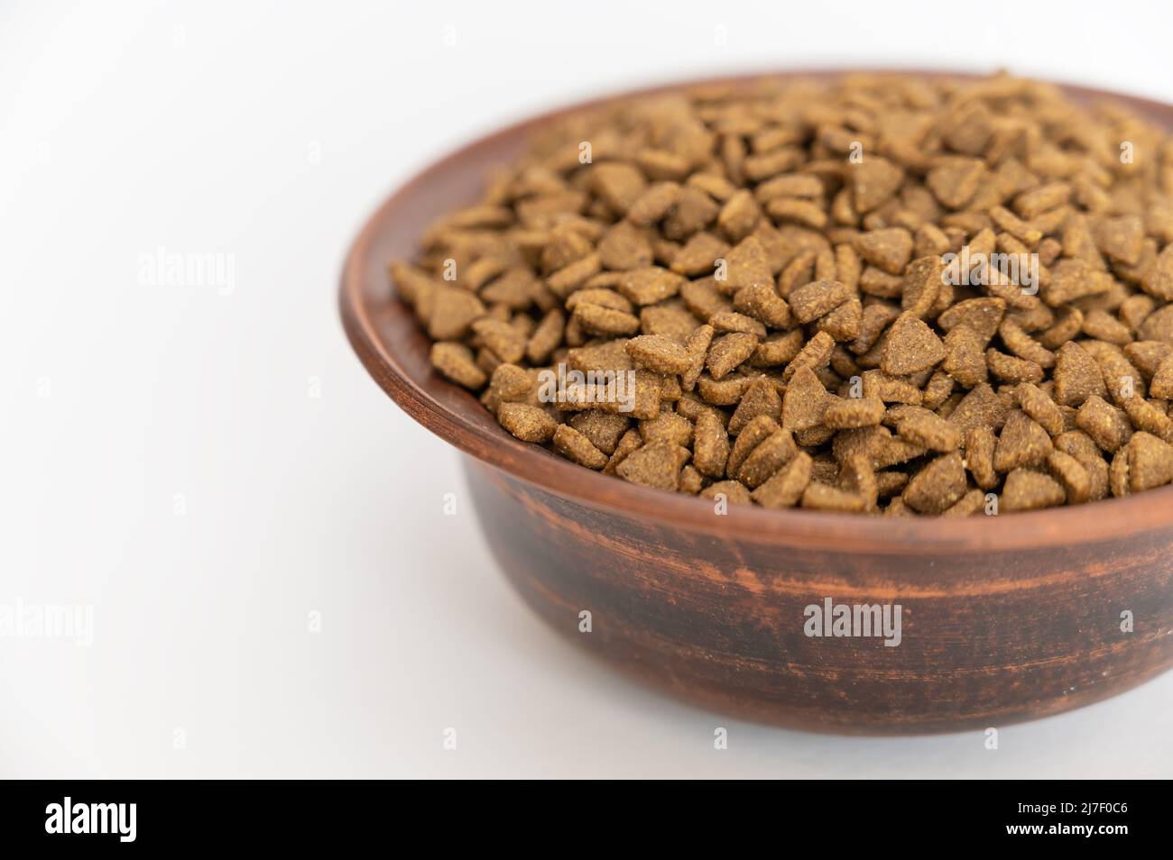 Pet food. Dry pelleted food in a brown clay bowl against a white ...