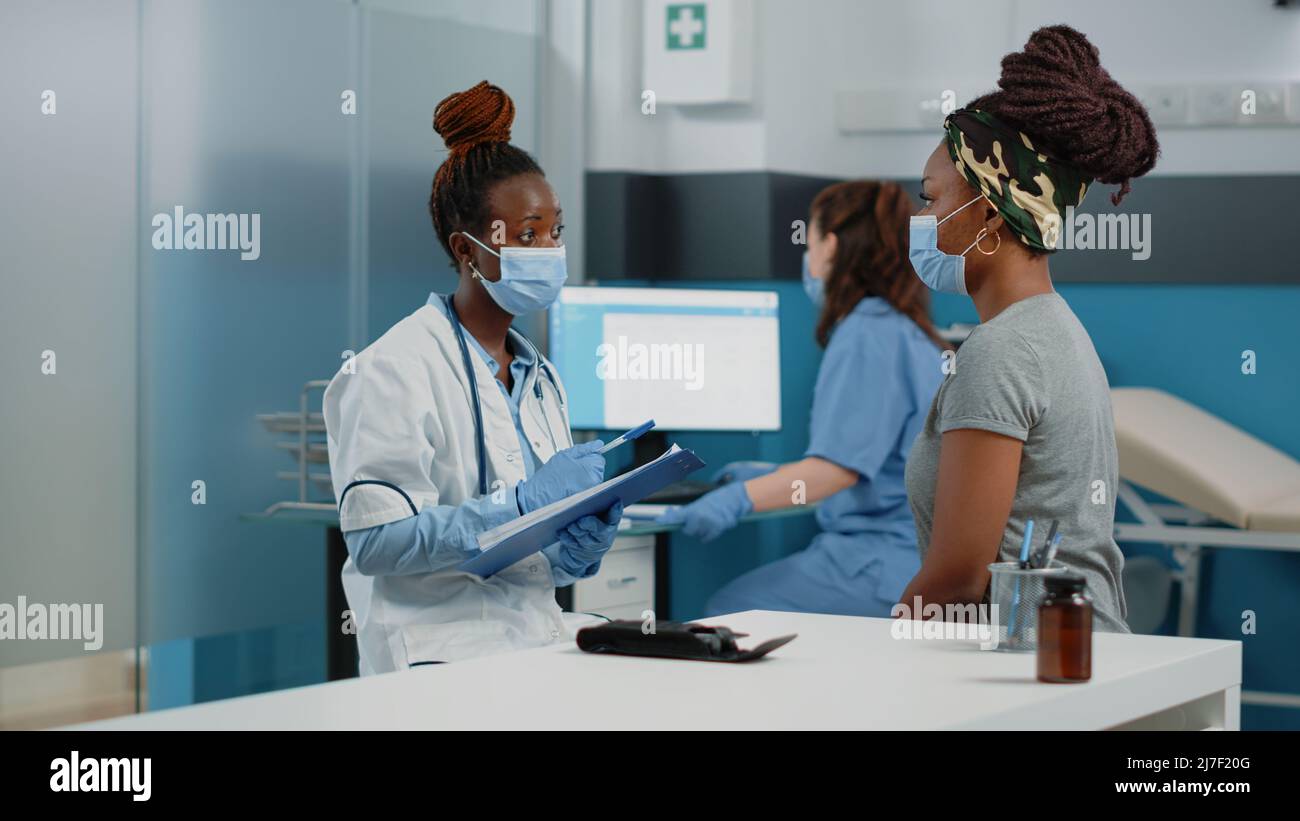 Doctor and patient with face masks talking about disease at annual ...