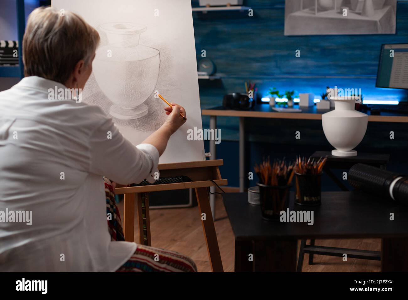 Focused retired art teacher doing creative artwork in pencil drawing ...