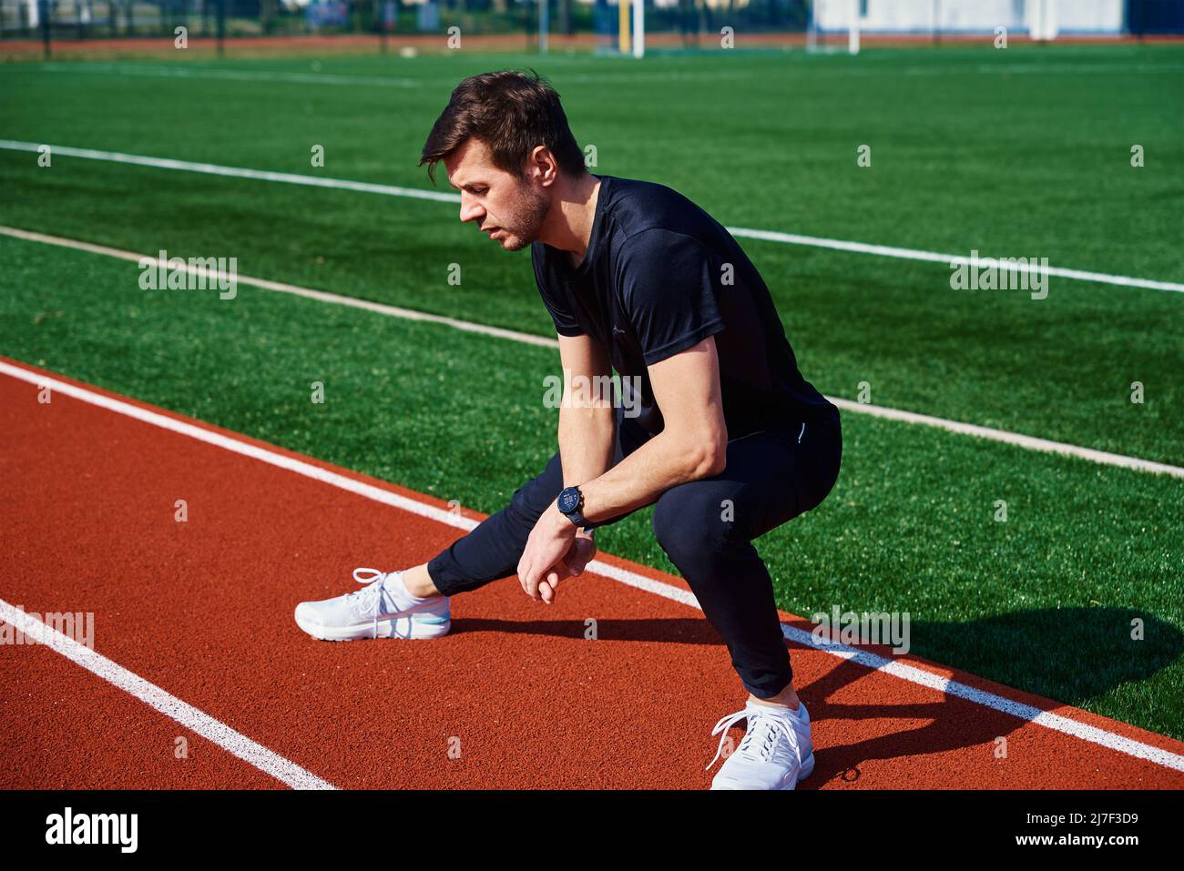 Man in sport clothers does a warm-up exercises at stadium track before ...