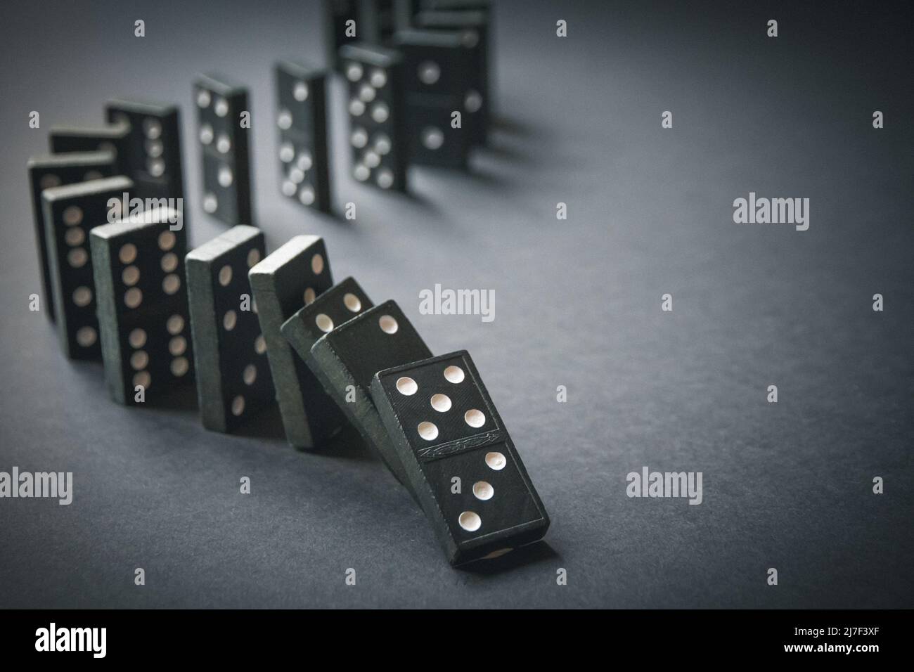 Black dominoes chain on a dark table background. Domino effect concept ...