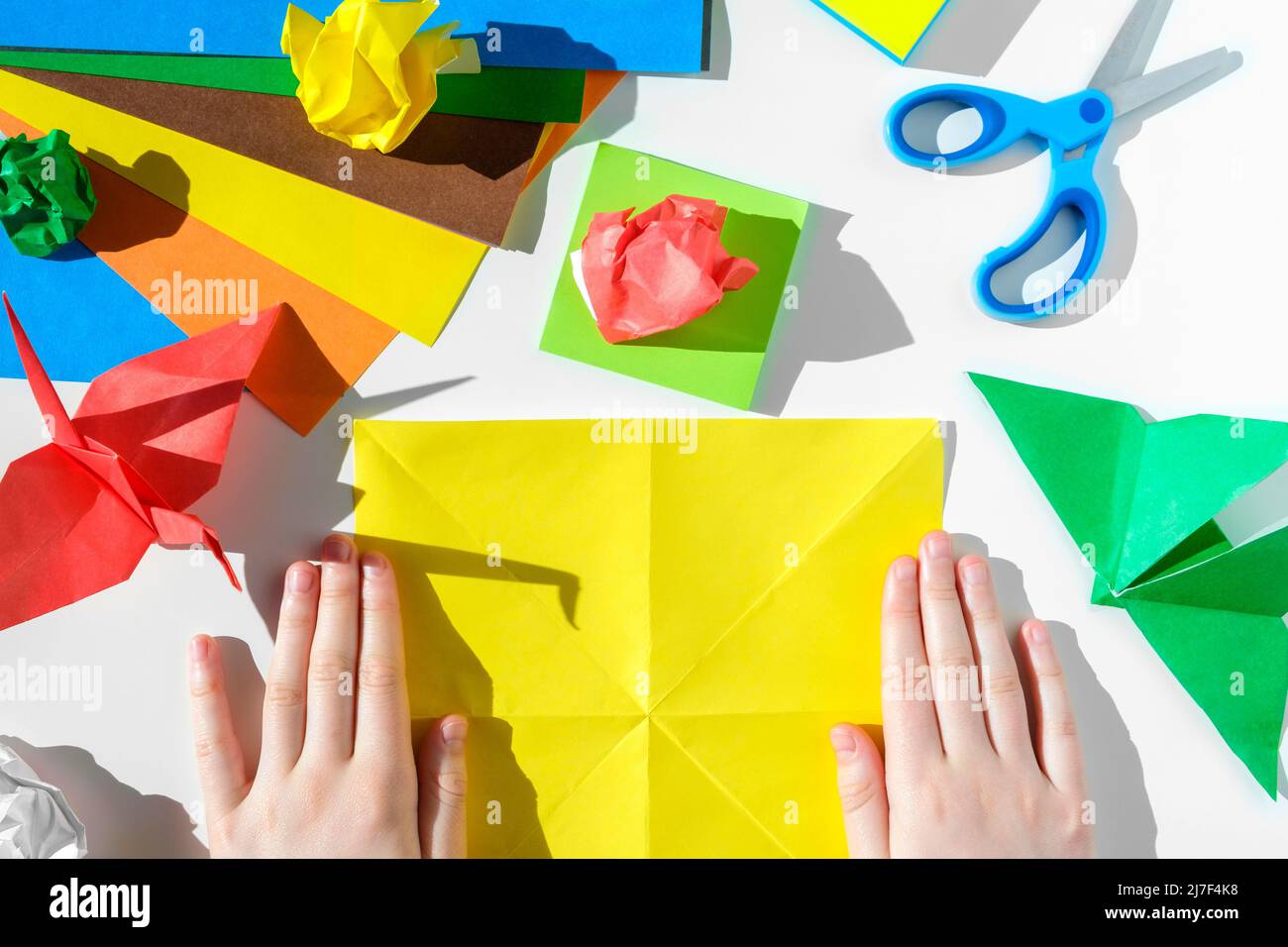 Paper crafts, scissors, colored paper sheets and scraps, on white table ...