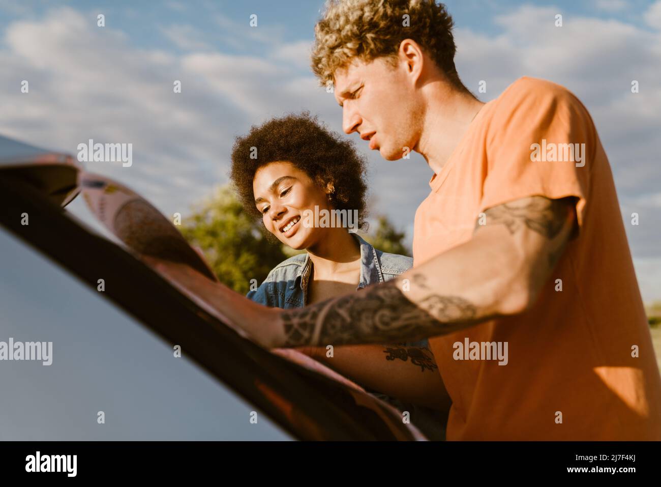 Young multiracial couple talking and examining map during car trip ...