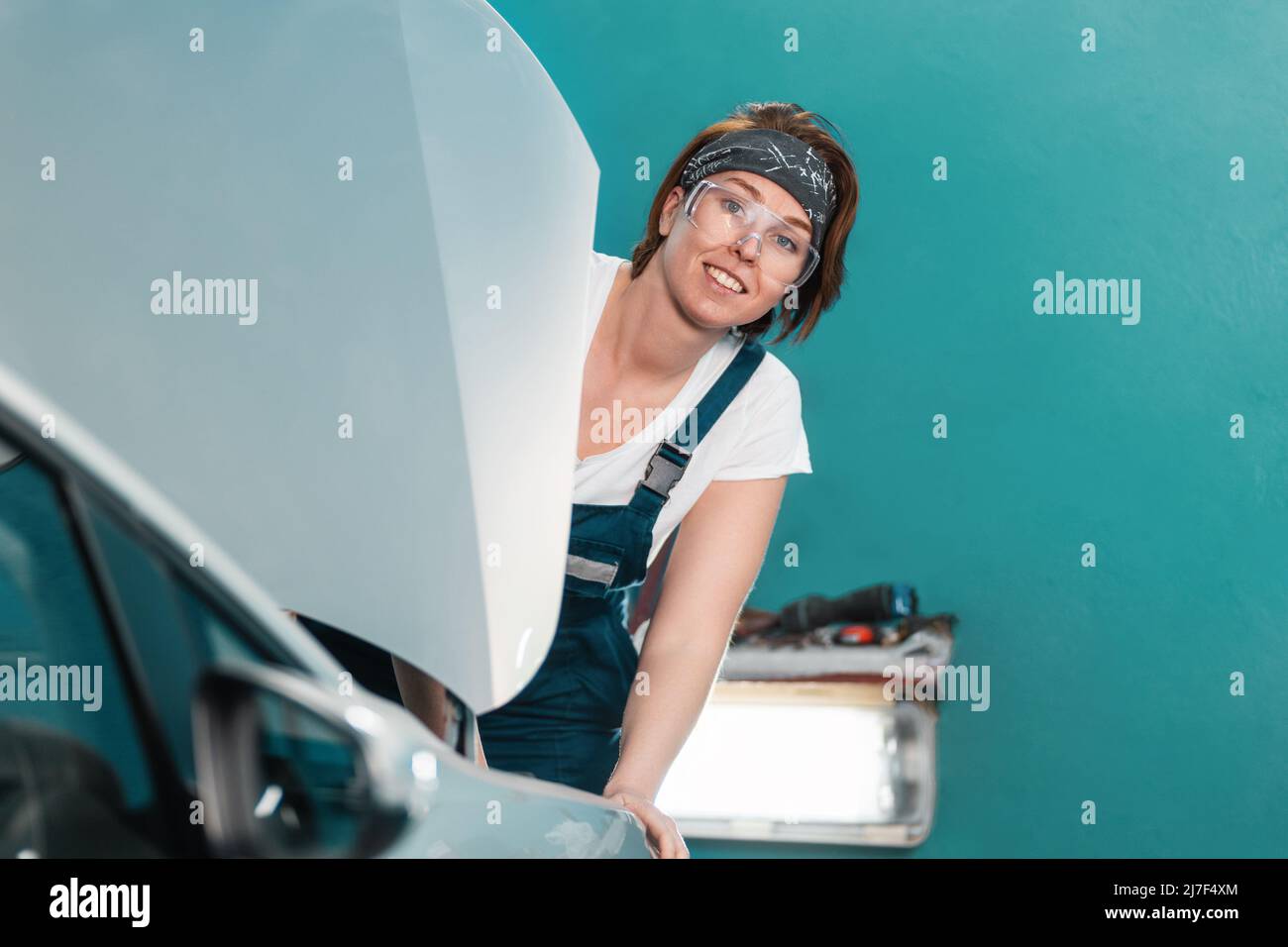A portrait of a young smiling female mechanic in glasses and coveralls ...