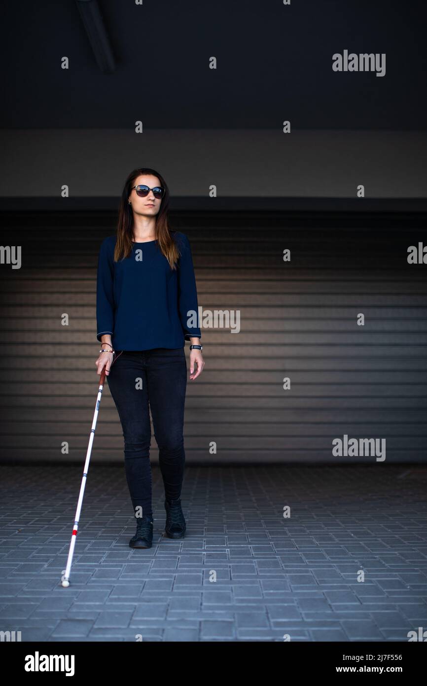 Blind woman walking on city streets, using her white cane to navigate ...