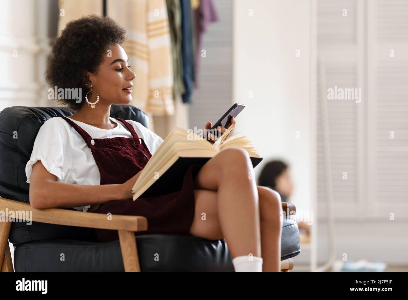 Young black woman using mobile phone while reading book at home Stock ...