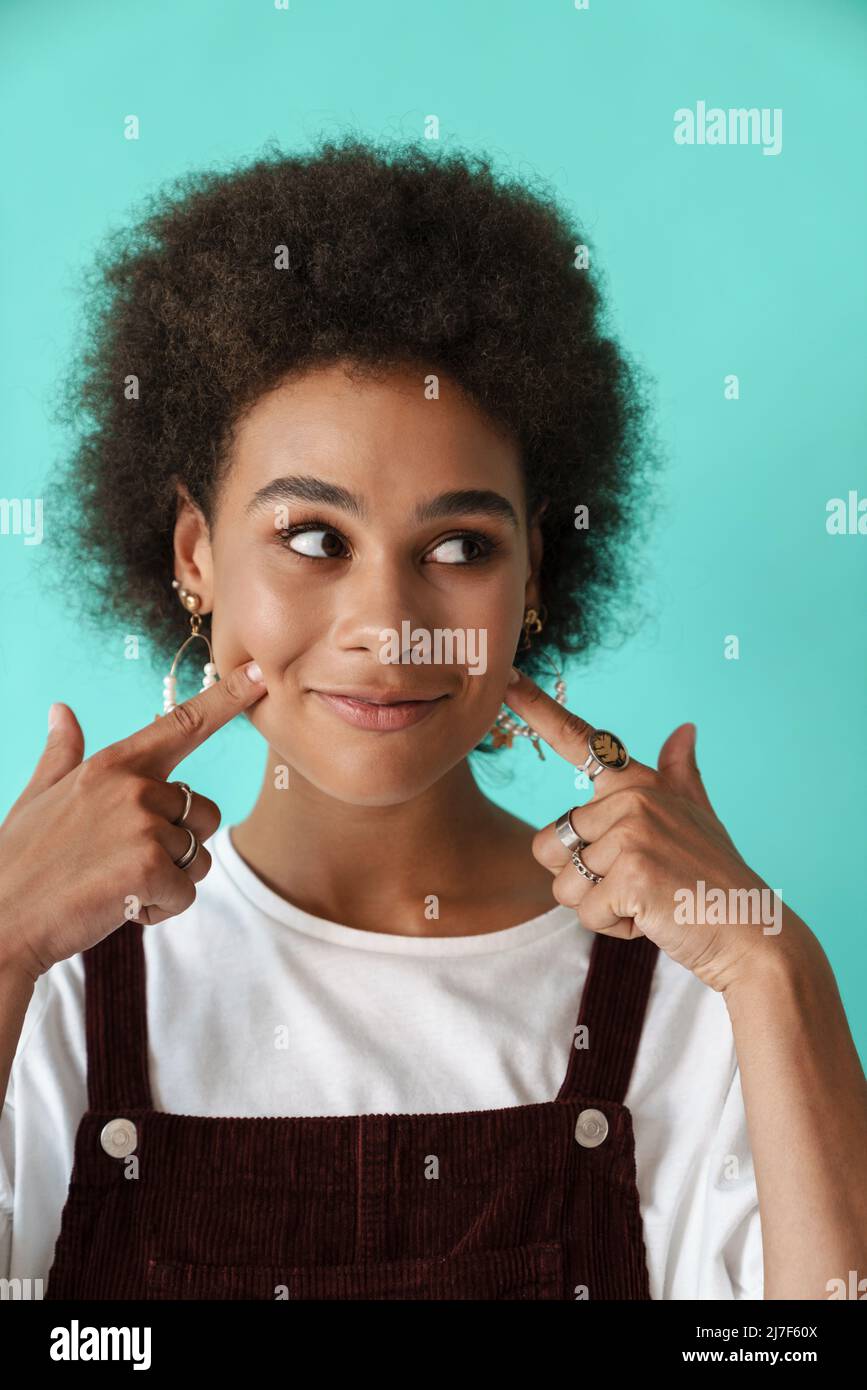 Young black woman smiling and pointing fingers at her cheeks isolated ...