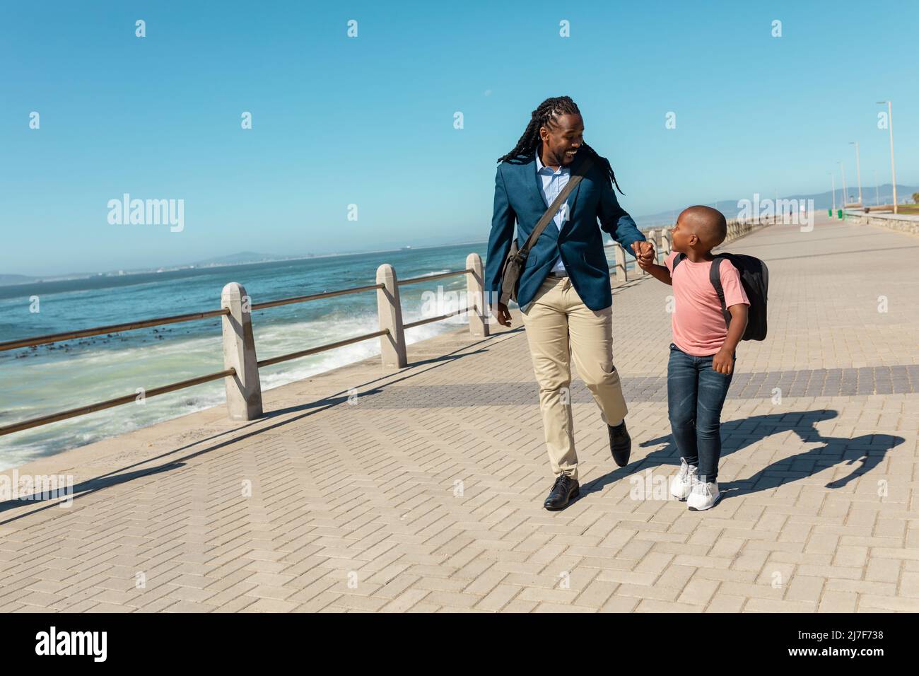 Happy african american father and son walking together on promenade ...