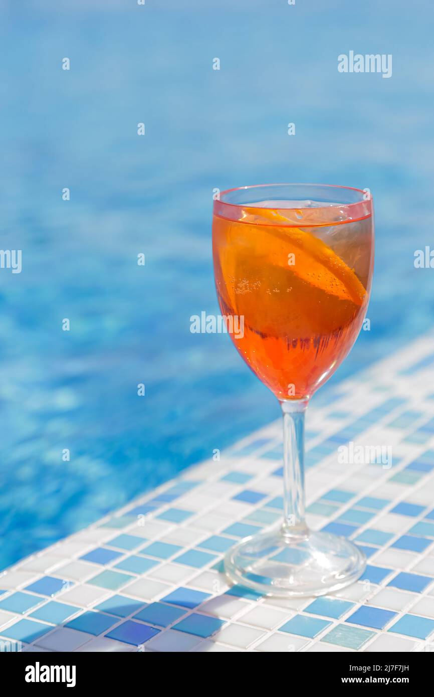 A transparent glass with an orange citrus cocktail stands on the edge ...