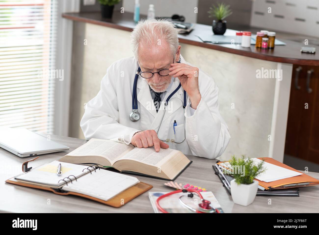 Senior doctor reading a textbook in medical office Stock Photo - Alamy