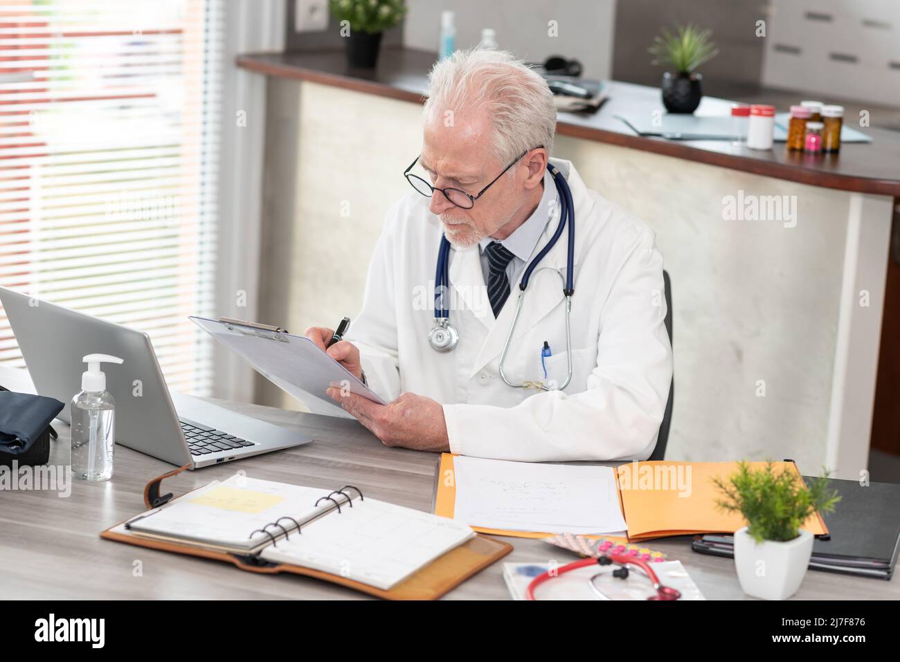 Senior doctor taking notes on clipboard in medical office Stock Photo ...