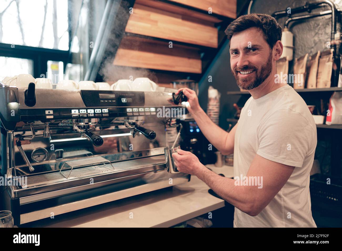 Cheerful Caucasian handsome man barista preparing coffee at machine ad ...