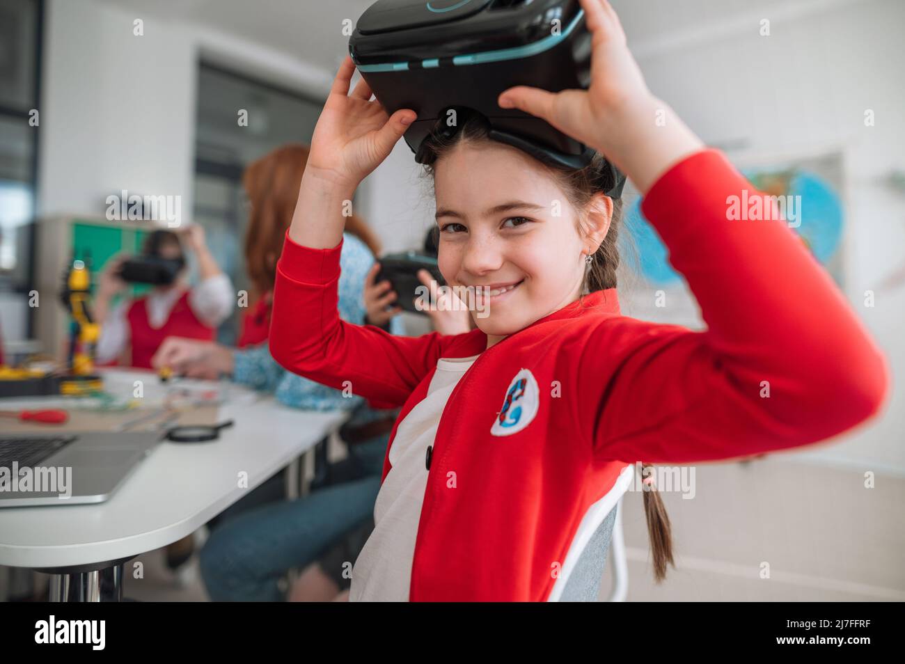 Happy schoolgirl wearing virtual reality goggles at school in computer ...