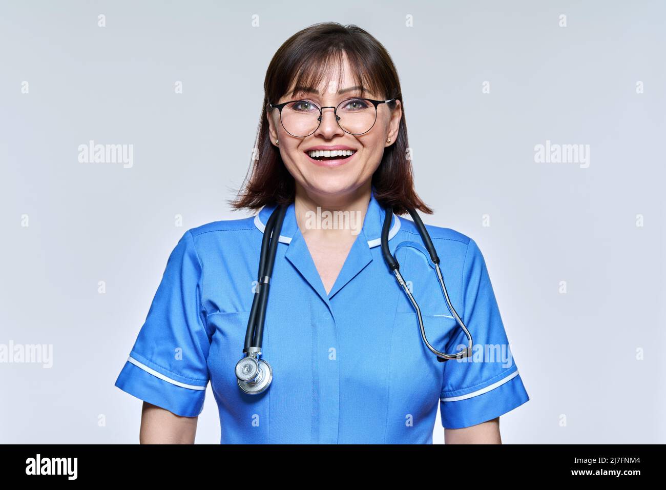 Headshot portrait of nurse in blue uniform looking at camera on light ...