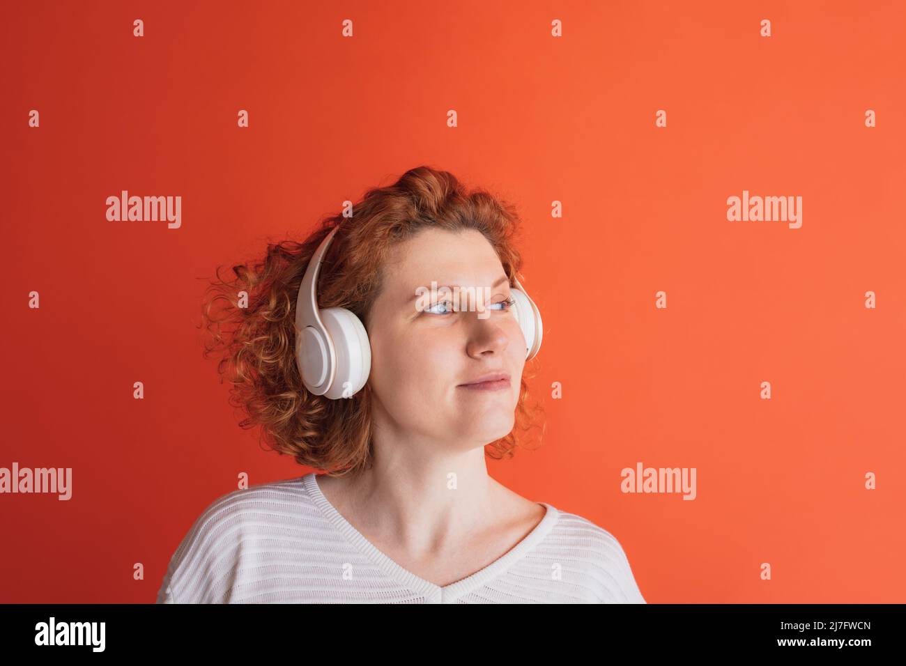 Portrait of calmly looking red-haired woman listening to music in white ...