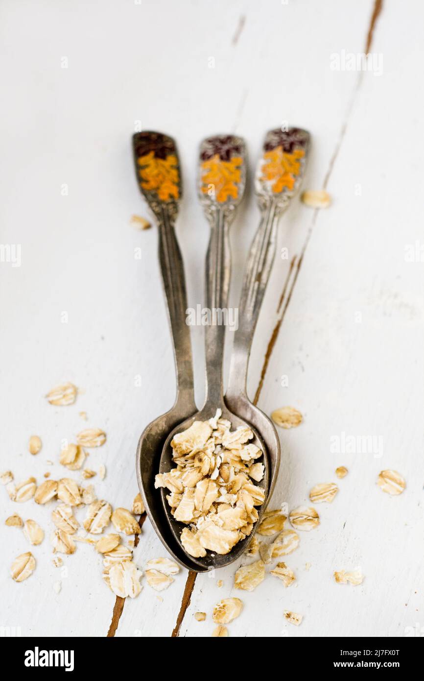 Three tablespoons of oatmeal lying on a white wooden background ...