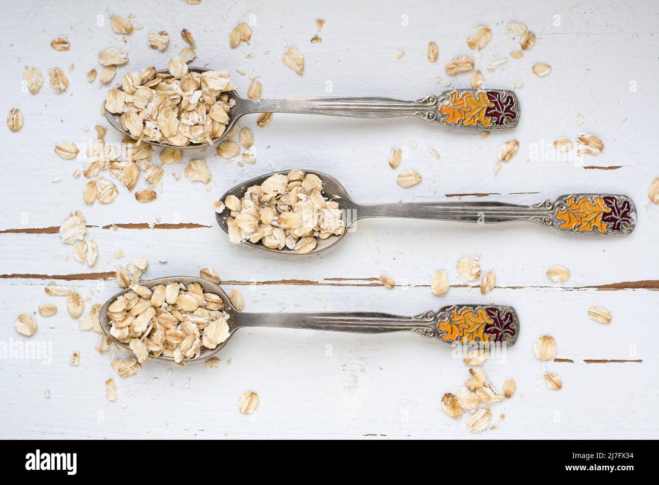 Three tablespoons of oatmeal lying on a white wooden background ...