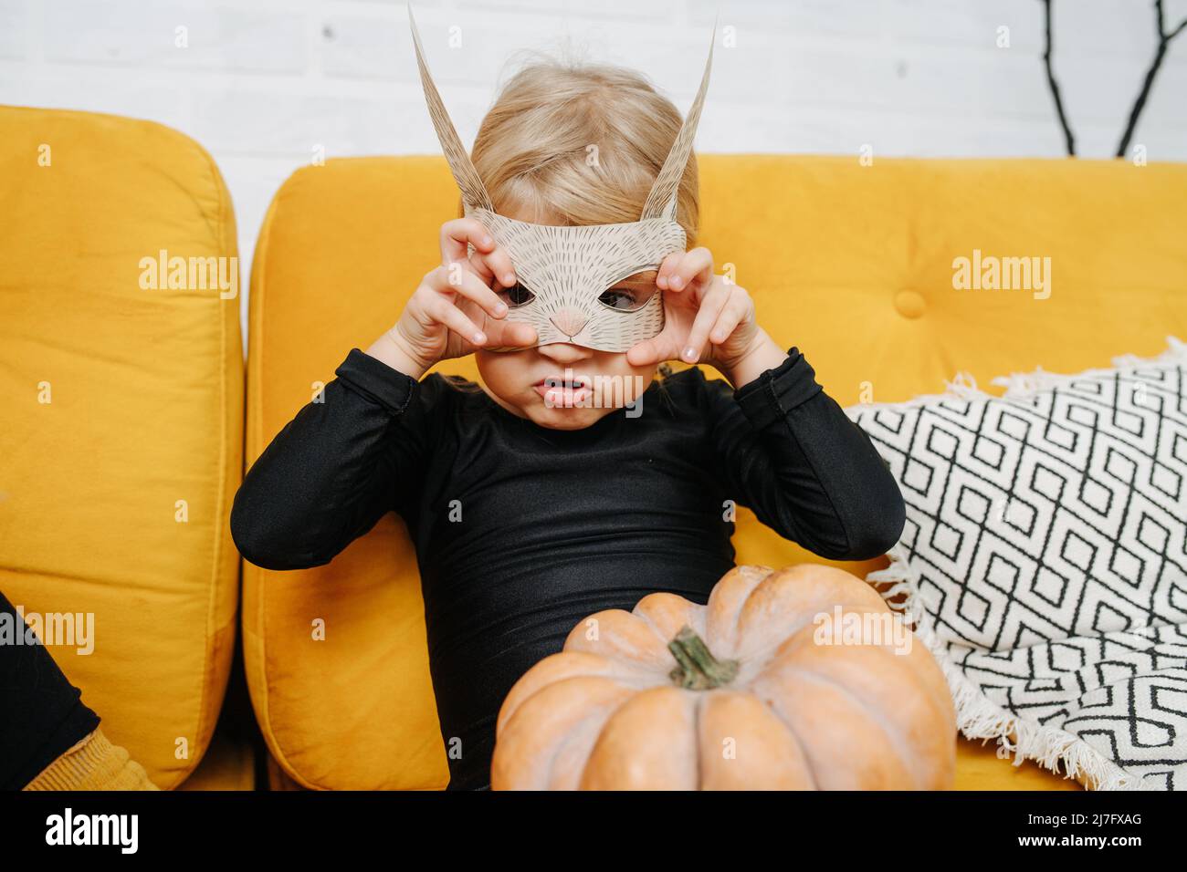 Little girl in paper rabbits mask dressed for halloween sitting on a ...