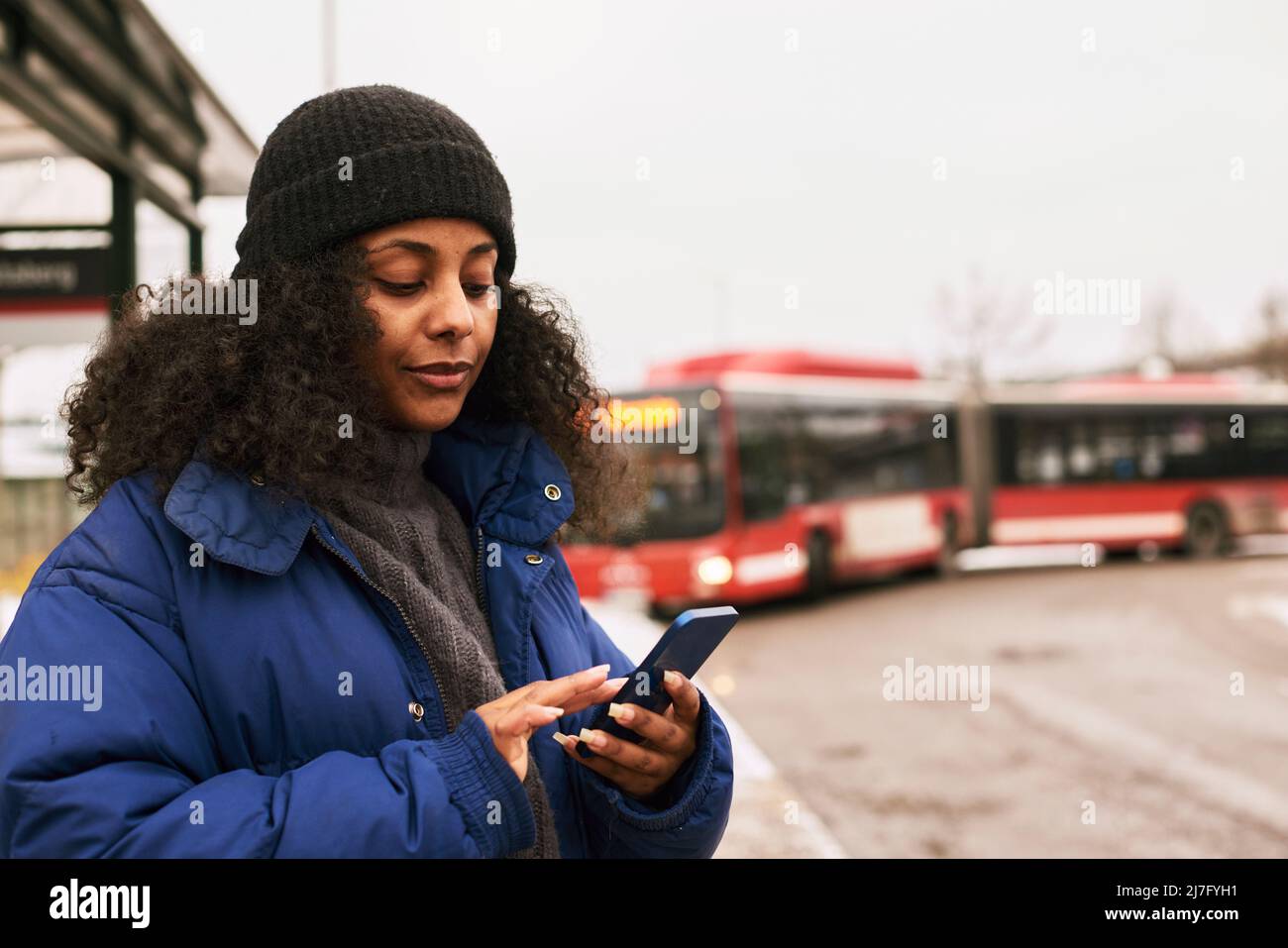 Woman using phone at bus stop Stock Photo - Alamy