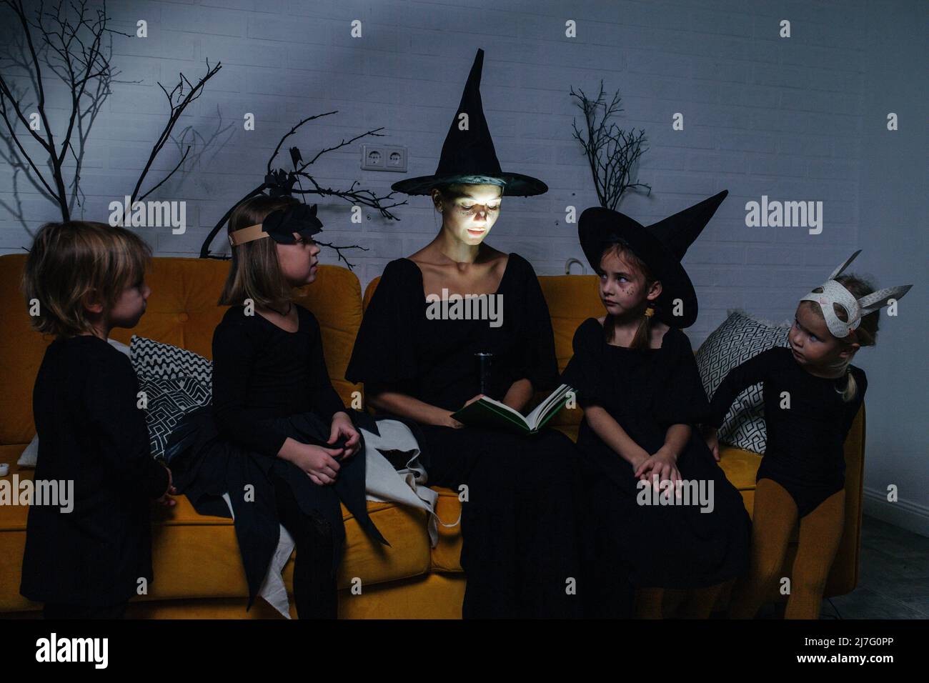 Mom reads scary story to children in a dark room, her face lit by a ...