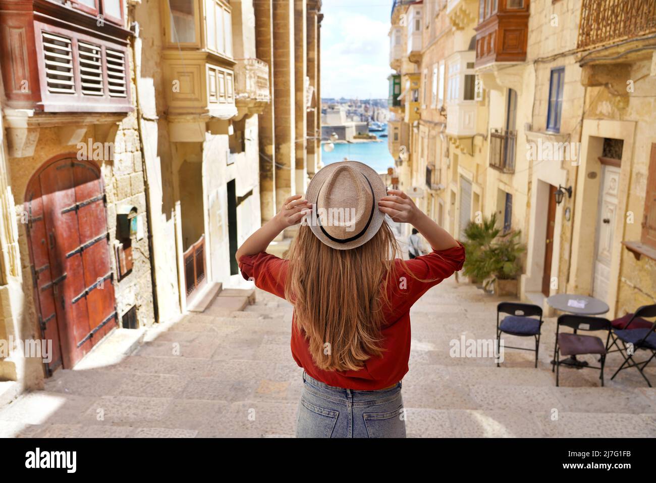 Tourism in Malta. Back view of tourist girl holding hat descends stairs ...